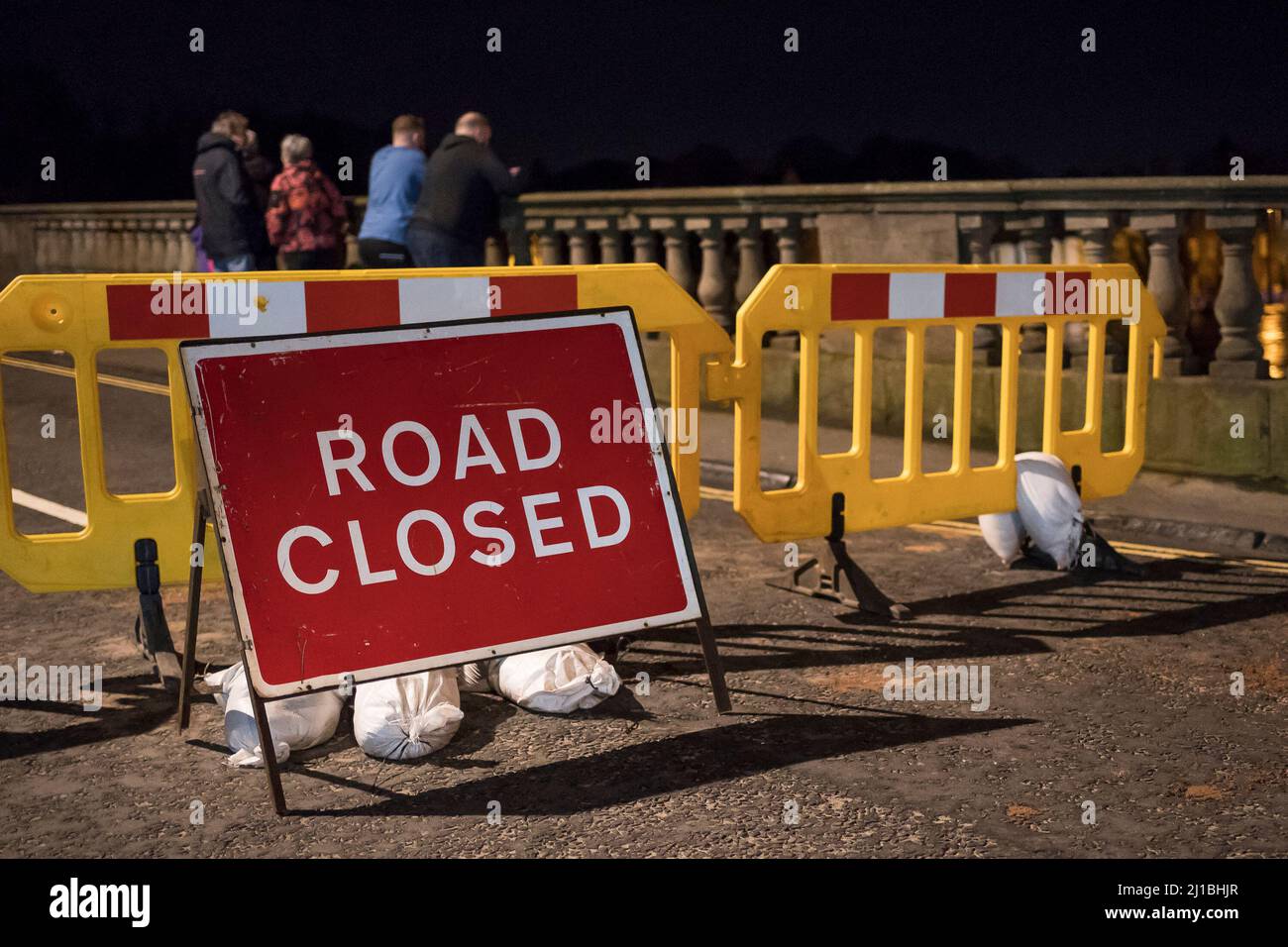 Road closed sign at night on a river bridge with people standing in the ...