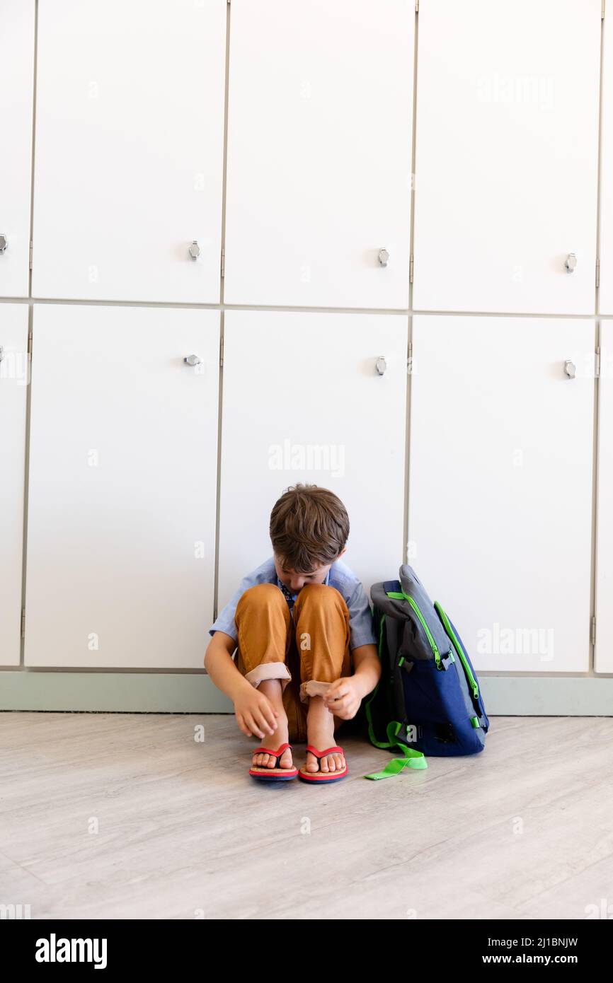 Sad caucasian elementary schoolboy wearing slippers while sitting on ...