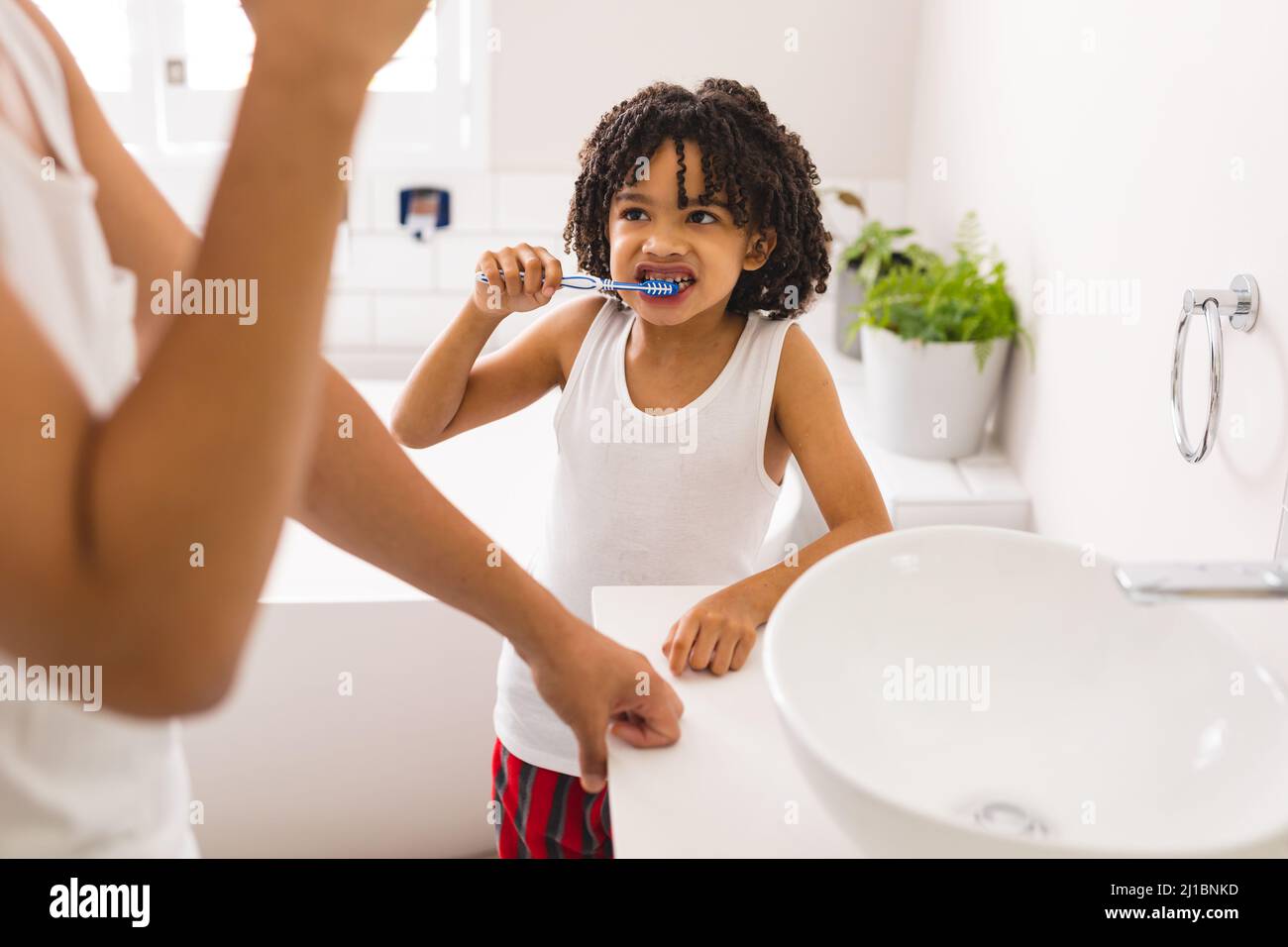 Hispanic boy brushing teeth while looking at father standing by sink in ...