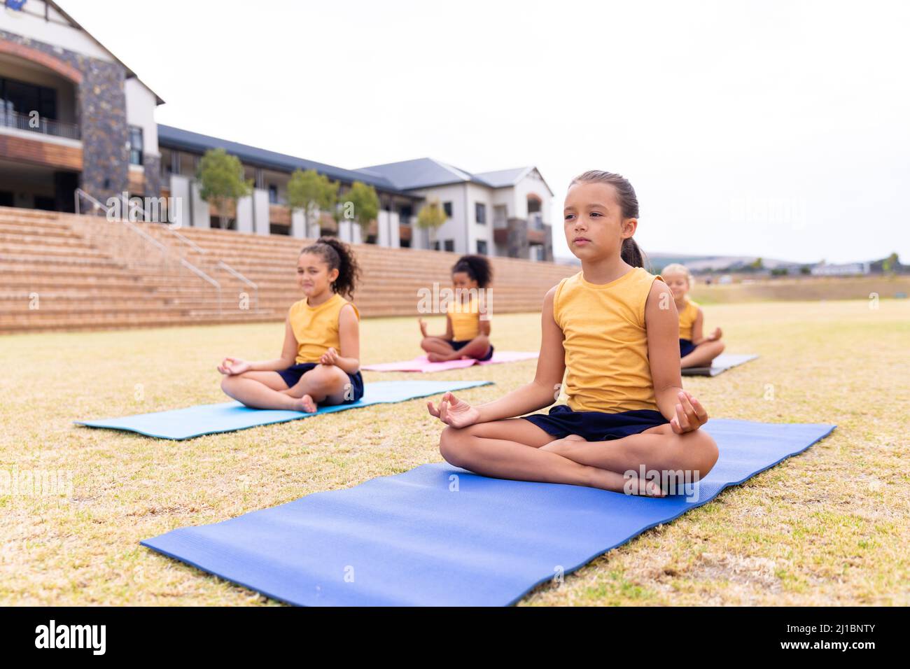 Multiracial elementary schoolgirls meditating while exercising on ...