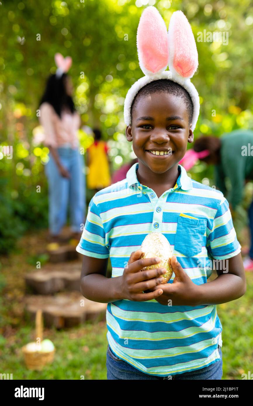Portrait of smiling african american boy in bunny ears holding easter ...