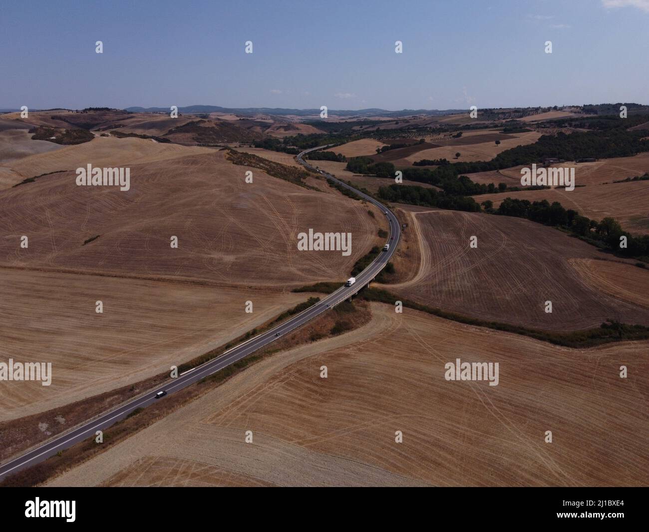 A bird's eye view of cars driving on an asphalt road on a landscape of yellow hills in Tuscany ...
