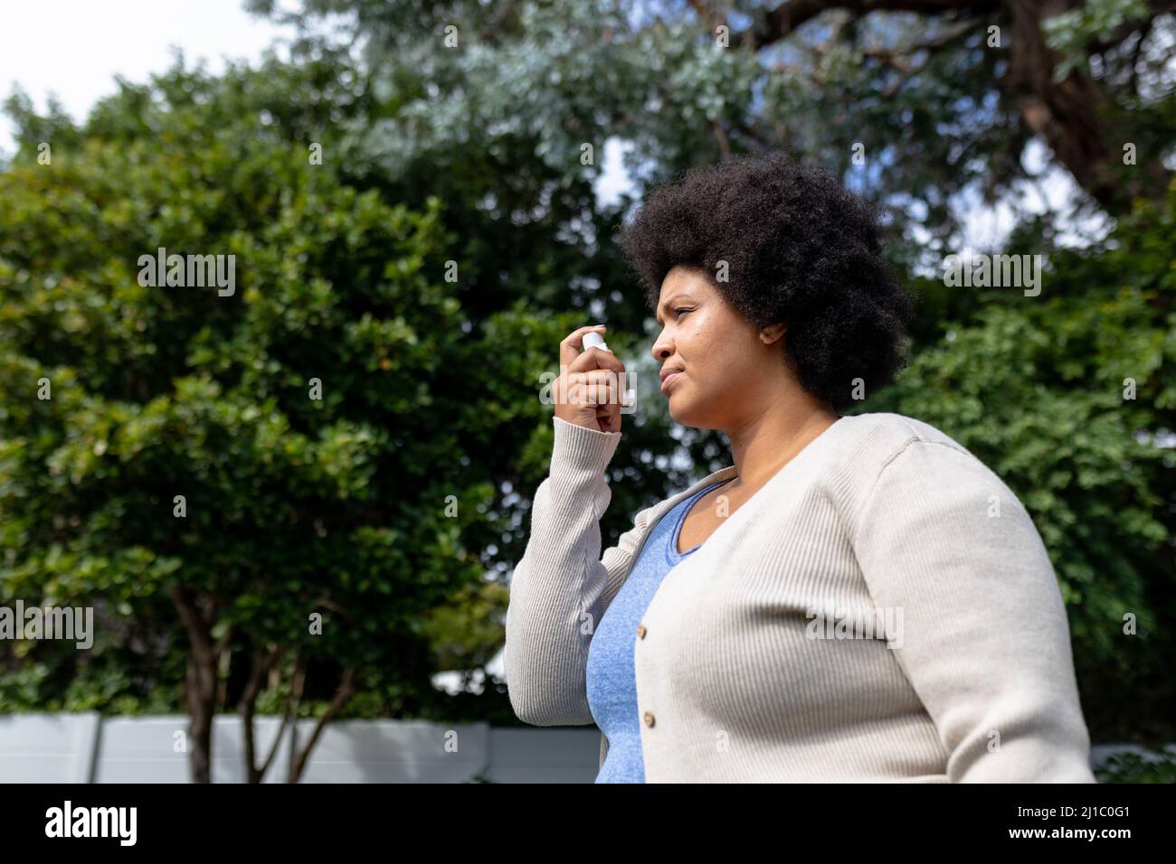 Side view of african american mid adult woman using asthma inhaler ...