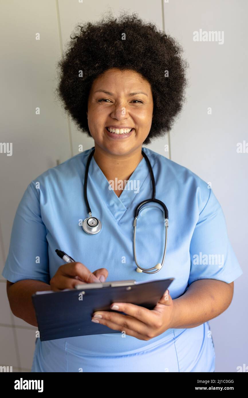 Portrait of smiling african american mid adult female nurse writing on ...