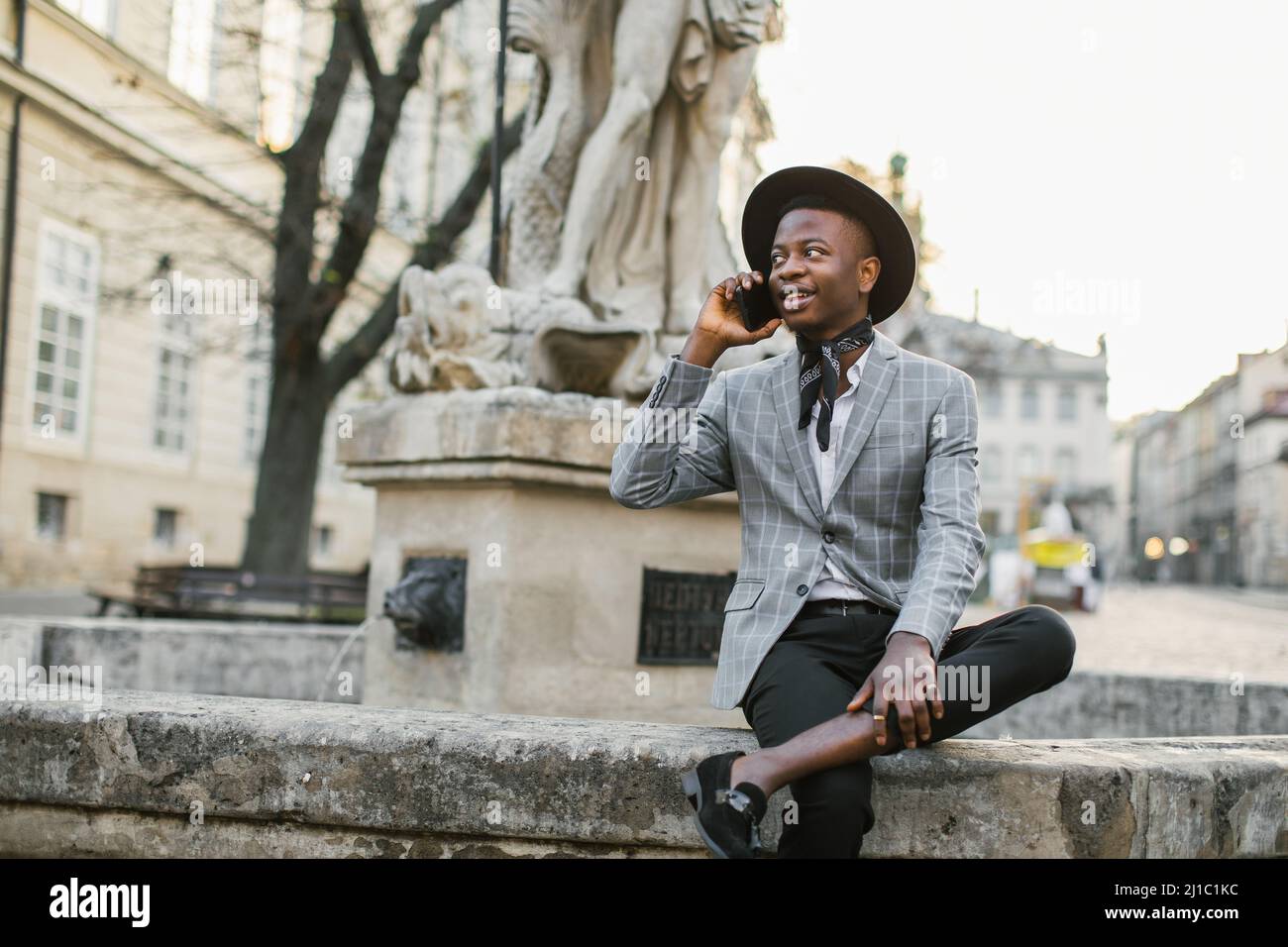 Smiling african man in stylish wear having mobile conversation while ...