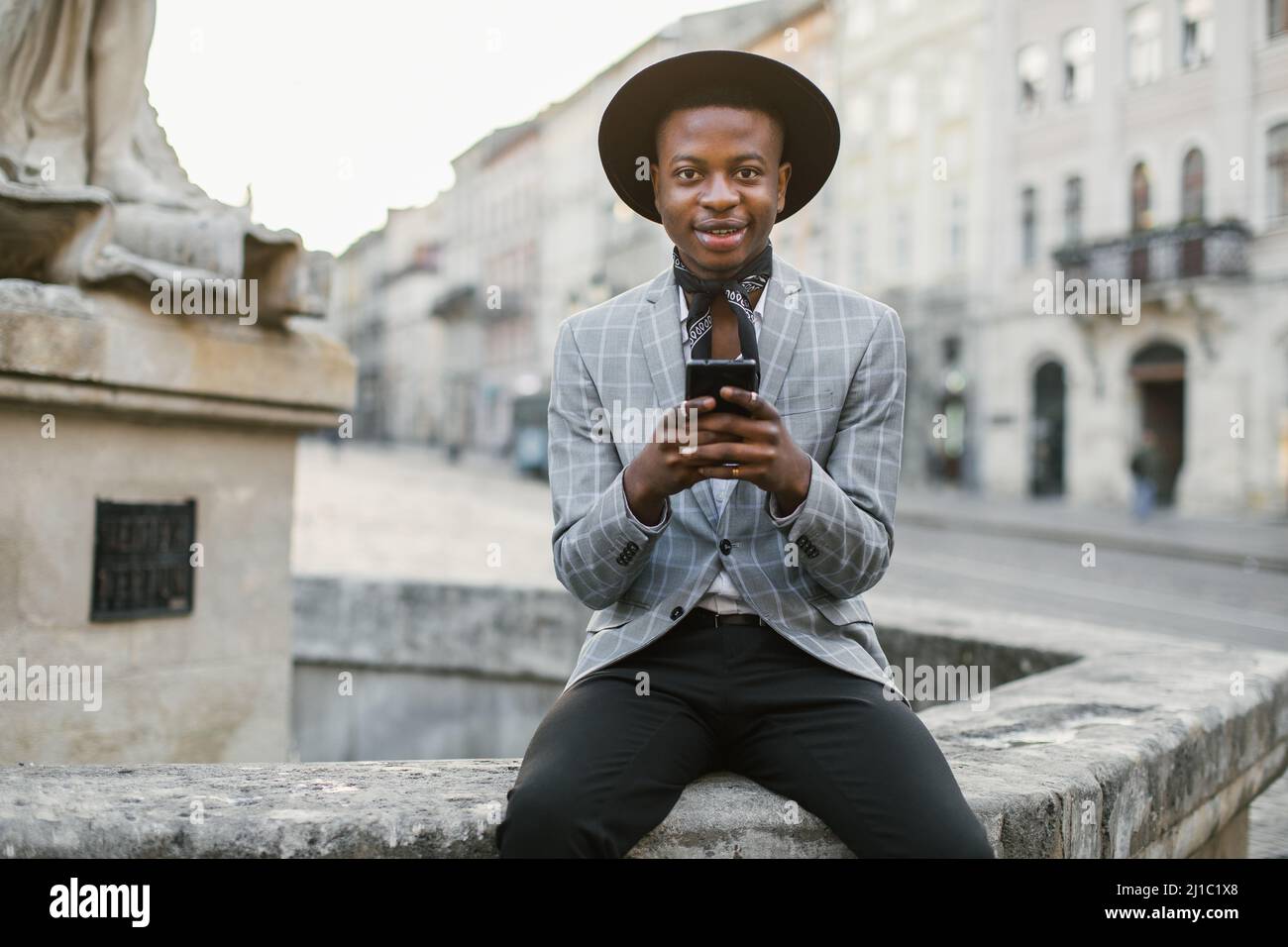 Happy African American Man In Suit And Hat Texting On Modern Smartphone