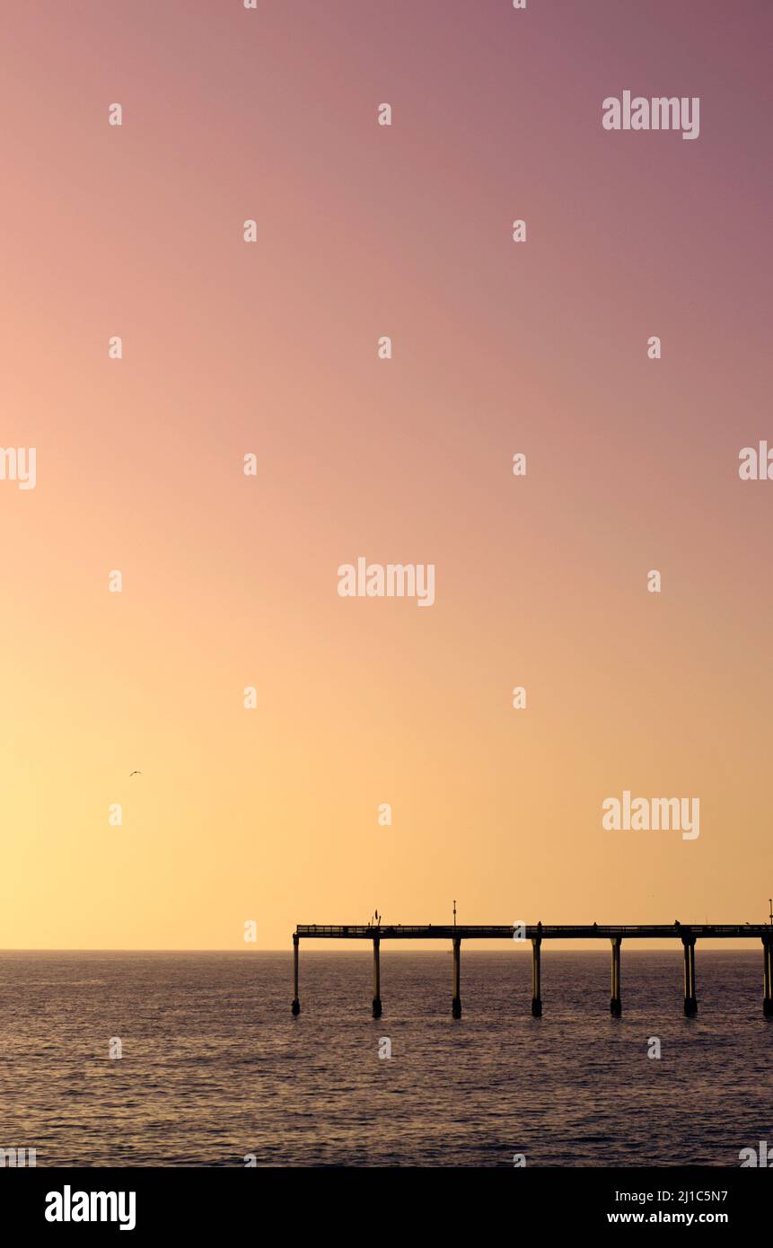The silhouette of a jetty stretched out in the ocean against a pink ...