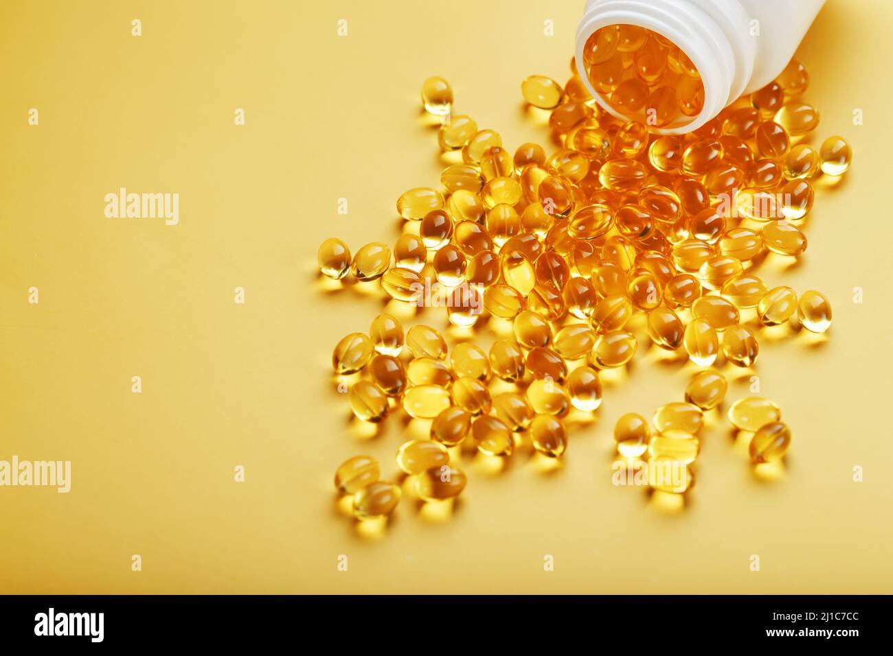 Gold Vitamin D3 capsules poured out of a jar on a yellow background ...