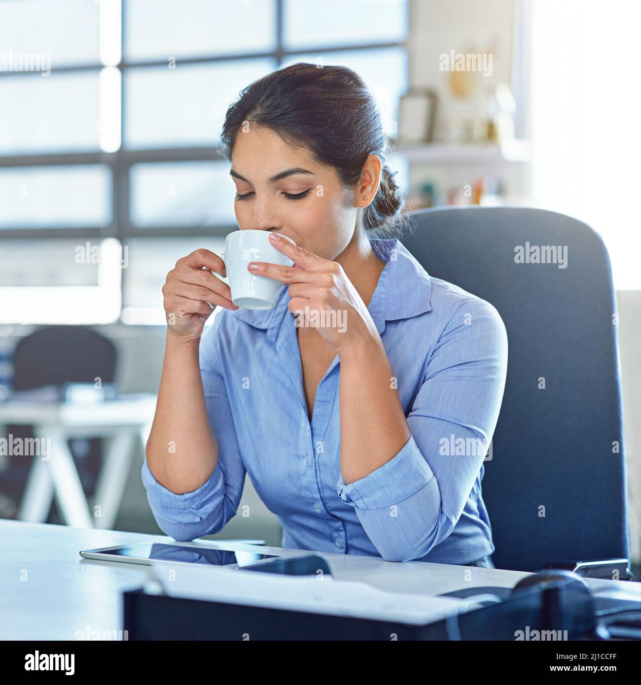 Taking a timeout from work. Shot of a young businesswoman drinking a ...