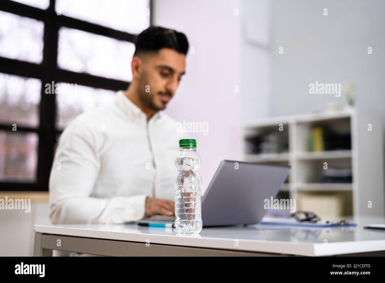 Water Bottle On Desk And Man In Foreground Using Computer Stock Photo ...