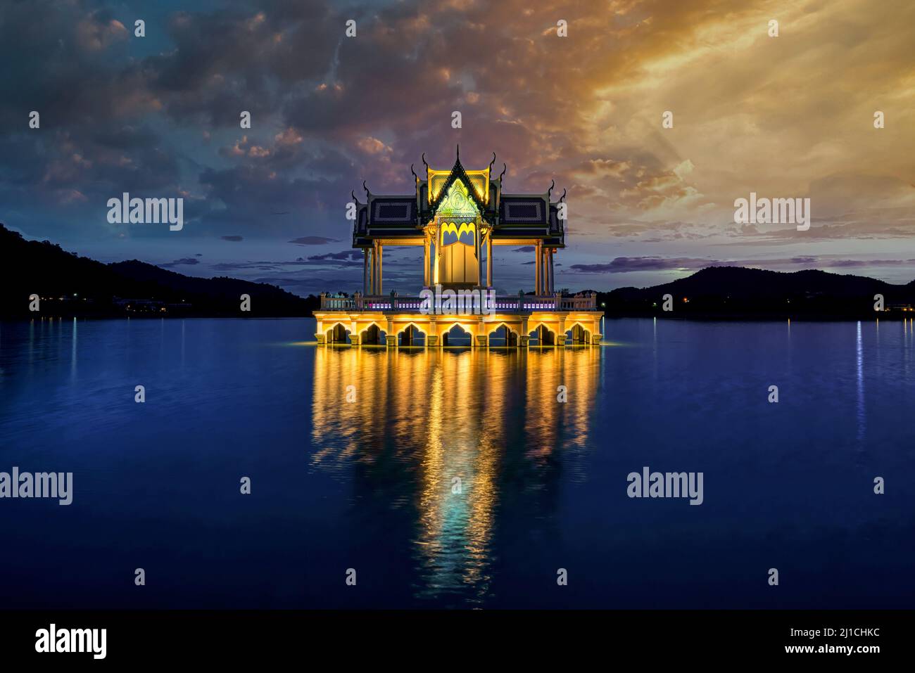 A scenic view of the Khao Tao Reservoir reflected in a lake on sunset ...