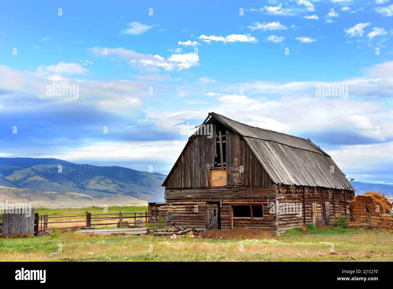 Rustic log barn has wooden roof and is in disrepair. Field behind barn ...