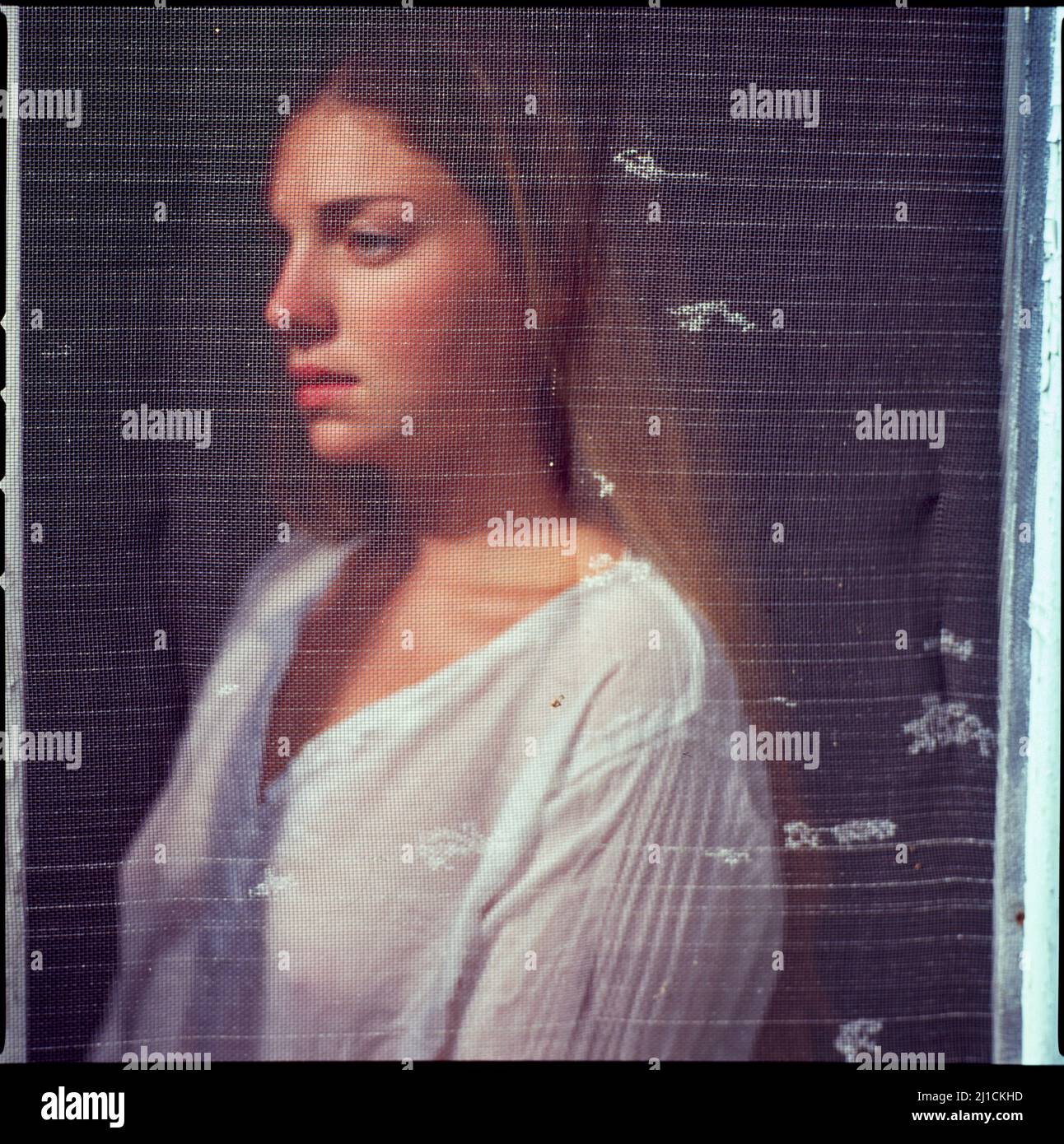 Young woman looking through screen door Stock Photo - Alamy
