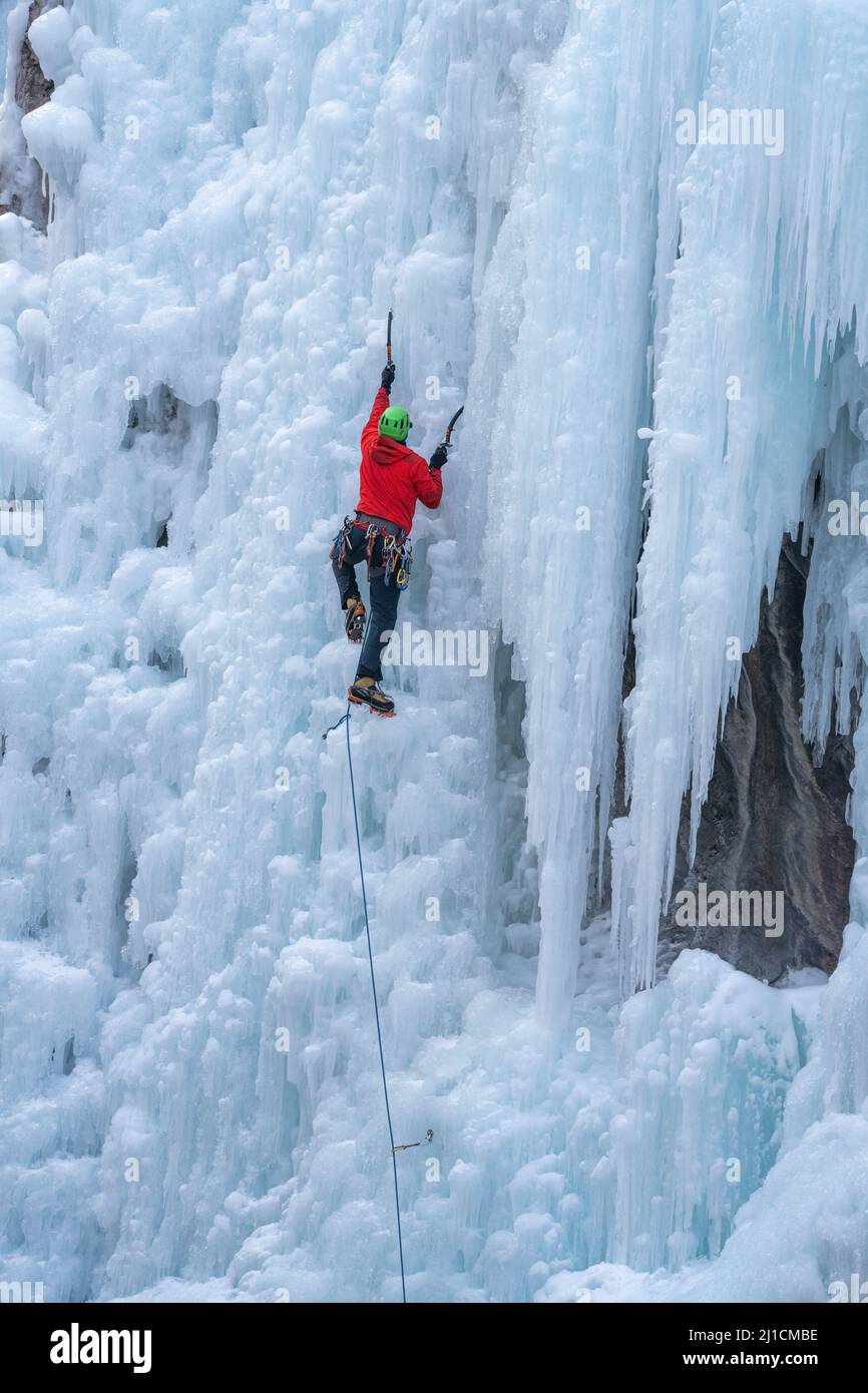 A male ice climber lead climbs an ice wall 160' high using ice axes and ...