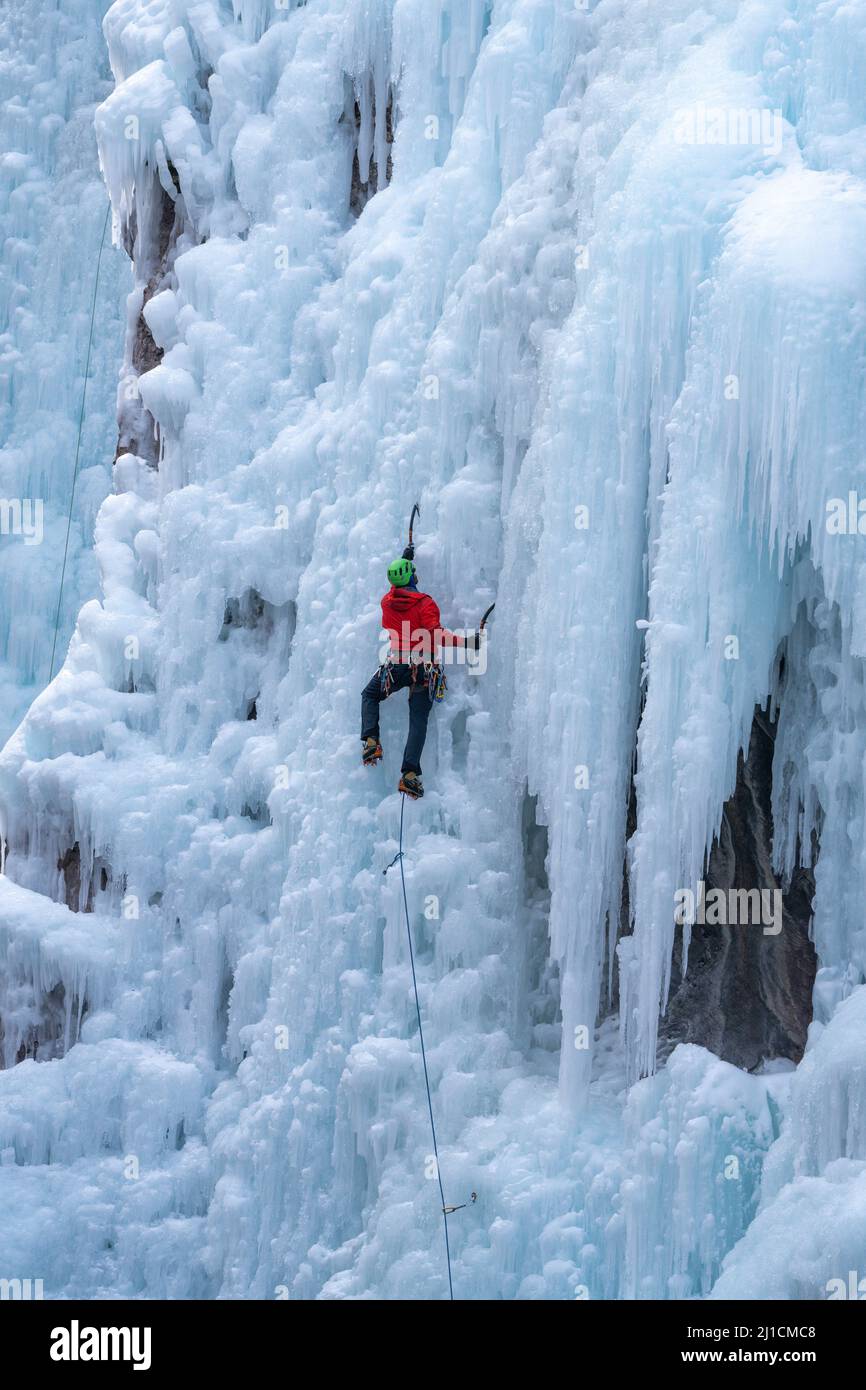 A male ice climber lead climbs an ice wall 160' high using ice axes and ...