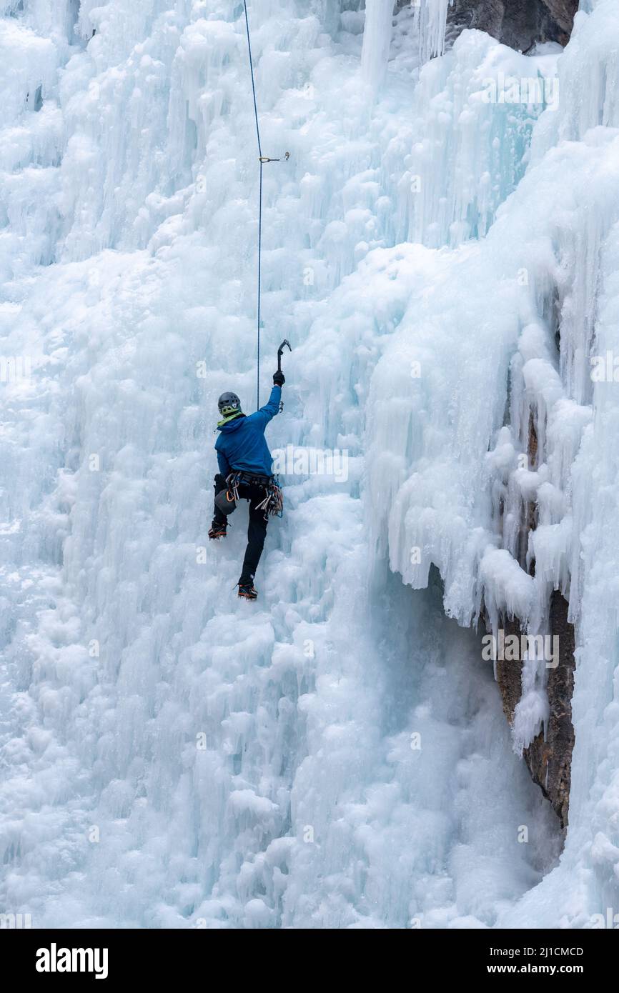 A male ice climber ascends an ice wall 160' high using ice axes and ...