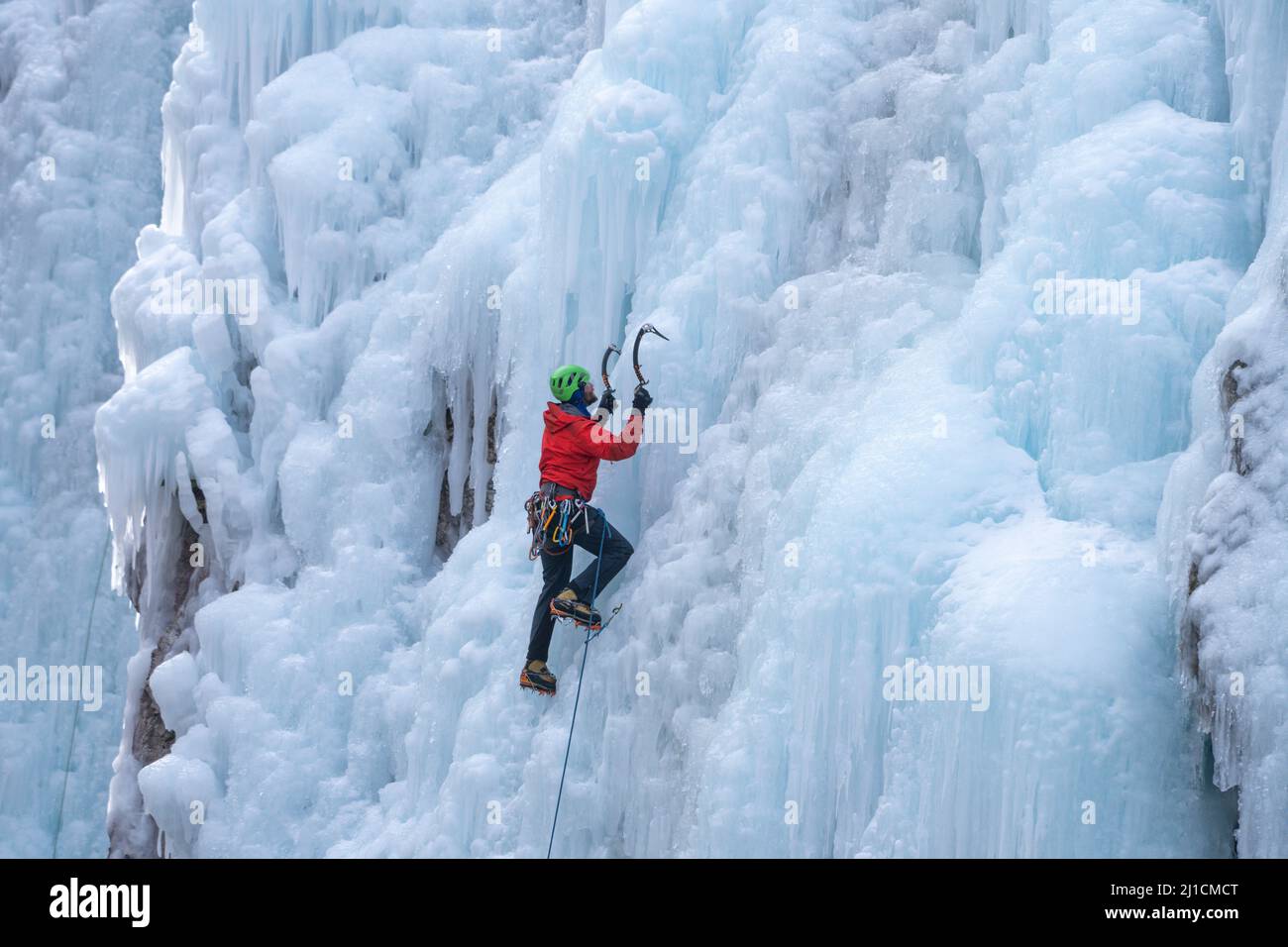 A male ice climber lead climbs an ice wall 160' high using ice axes and ...