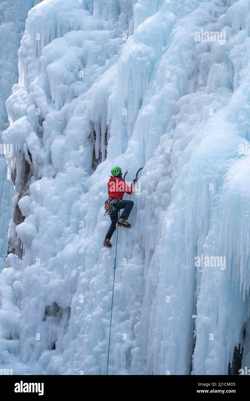 A male ice climber lead climbs an ice wall 160' high using ice axes and ...