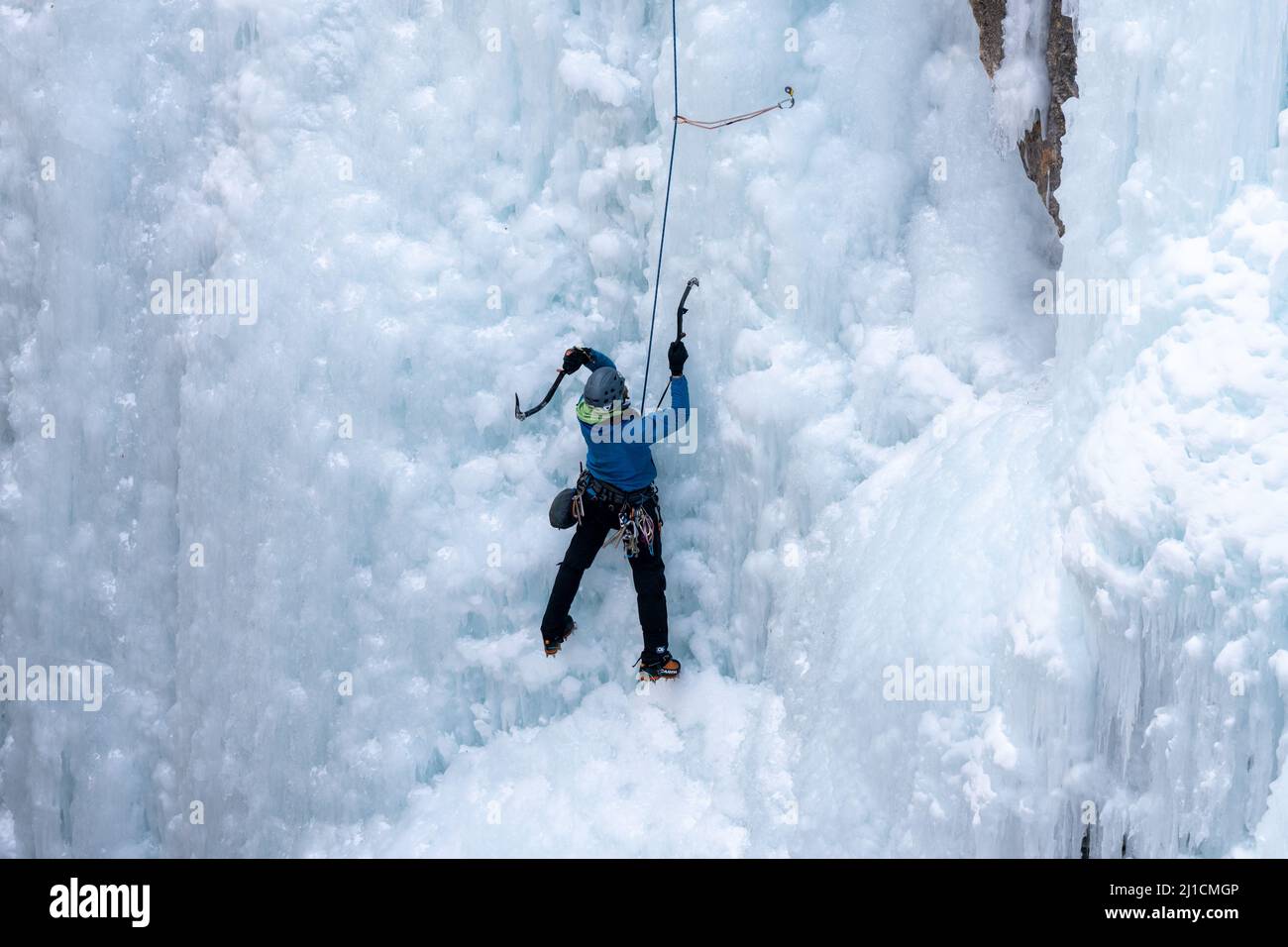 A male ice climber ascends an ice wall 160' high using ice axes and ...