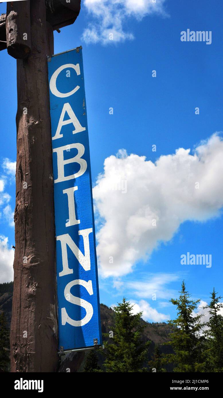 Blue wooden sign is attached to a log pole. Sign has lettering that ...