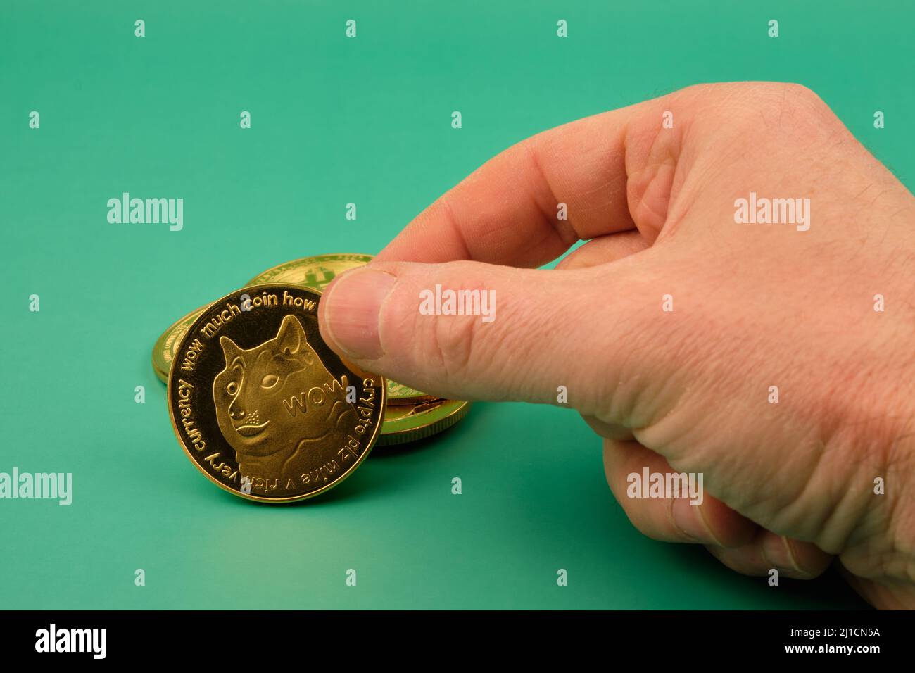 A man's hand holding a dogecoin with a green background. Photograph in ...