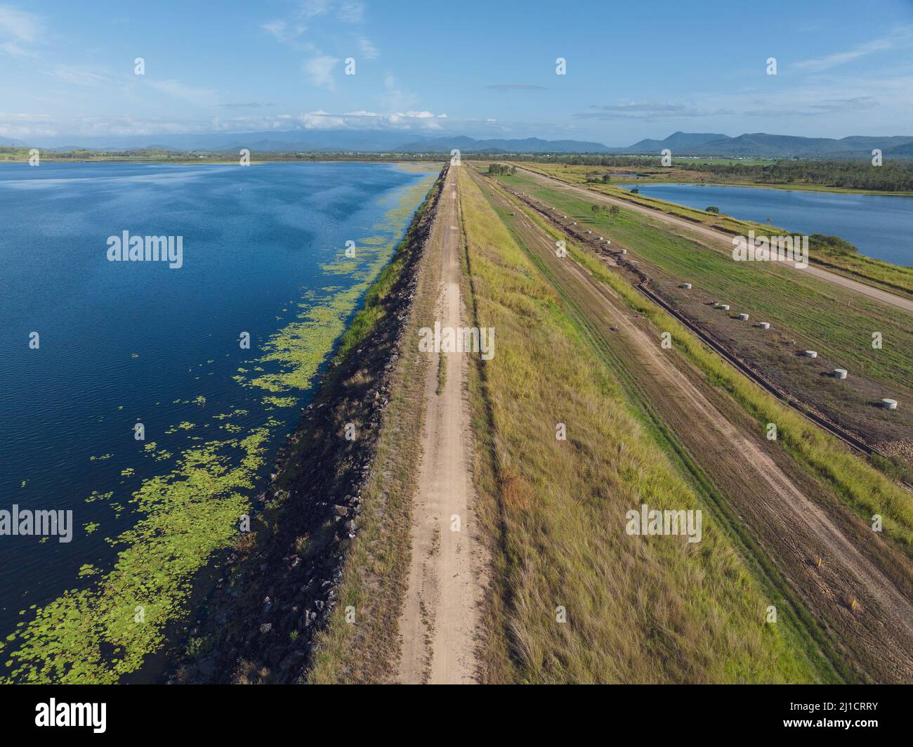 Droning along a dam wall with aquatic plants edging the water and a ...