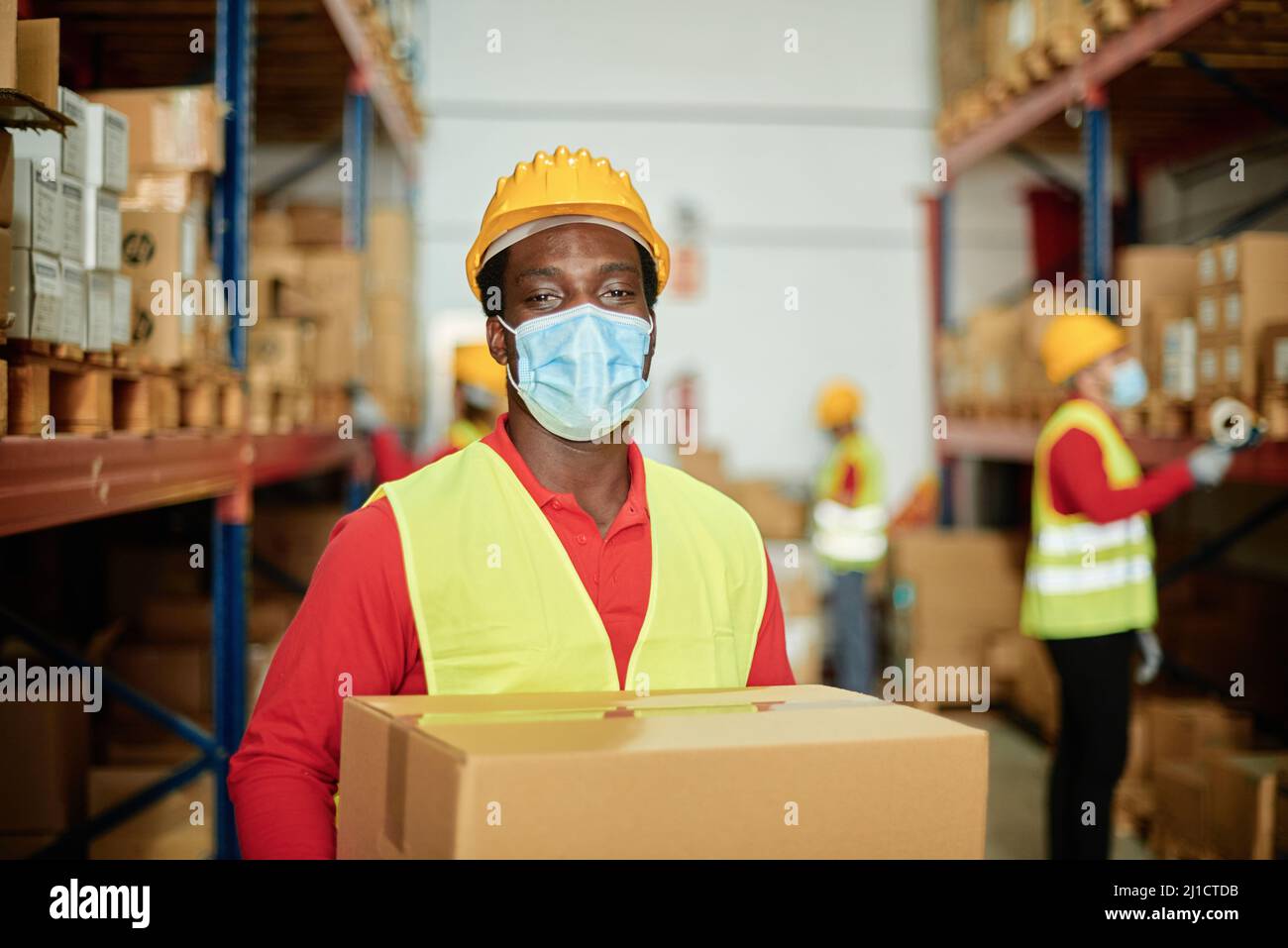 Afro male worker loading a box in a transport warehouse wearing a ...