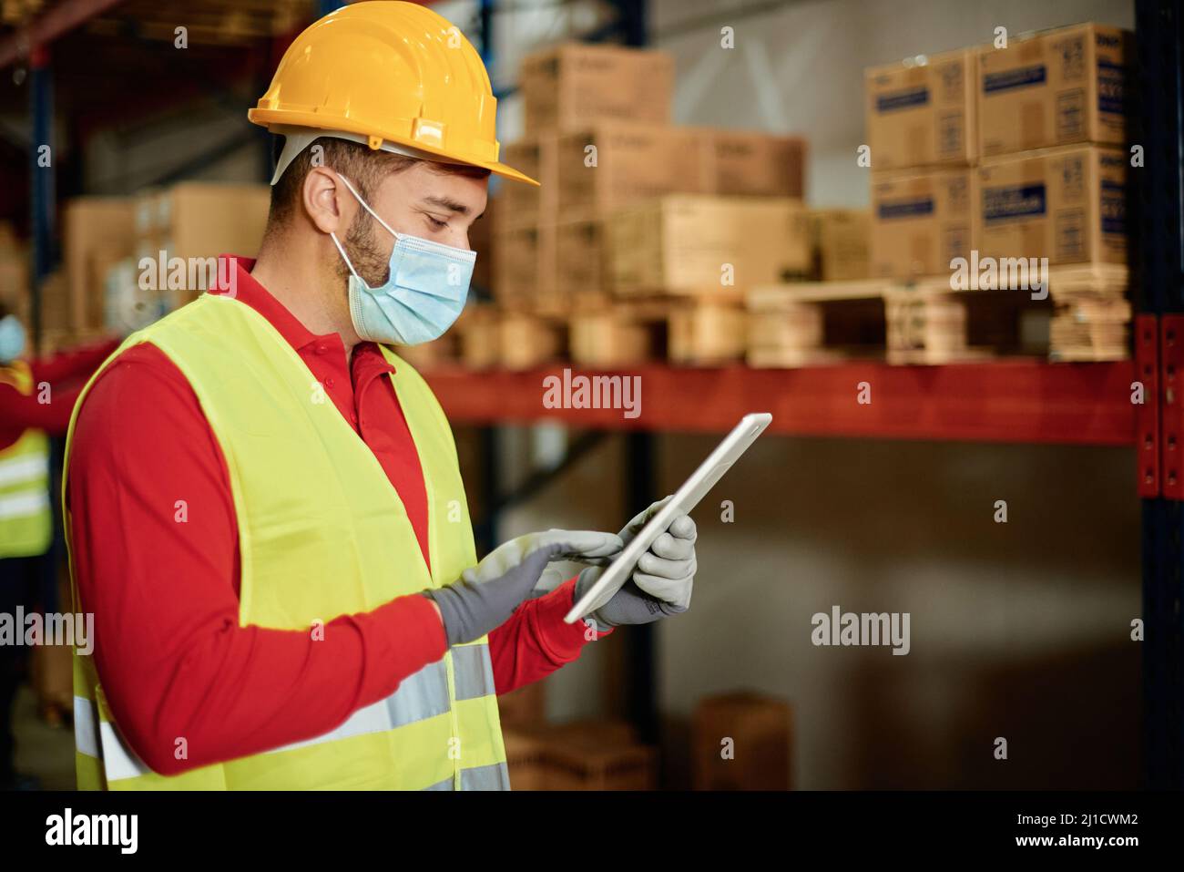 Caucasian worker man using tablet inside warehouse while wearing safety ...