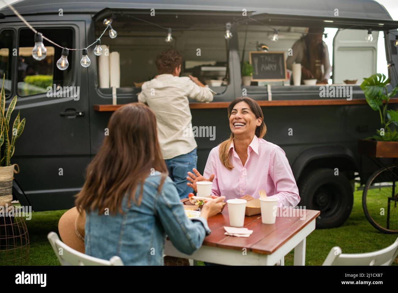 Cheerful women eating street food near truck Stock Photo - Alamy
