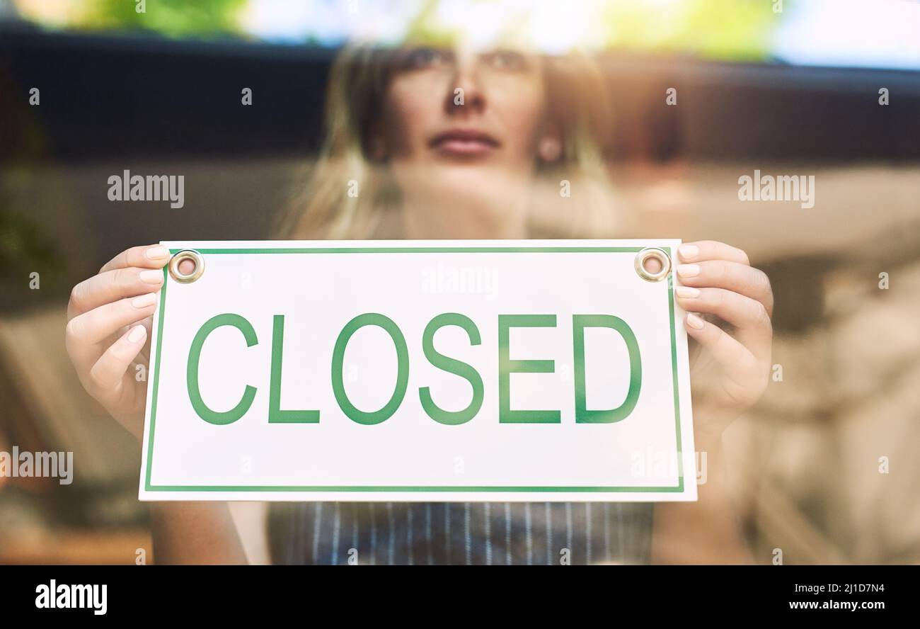 Sorry were closed. Shot of a woman putting up a closed sign in a bar ...