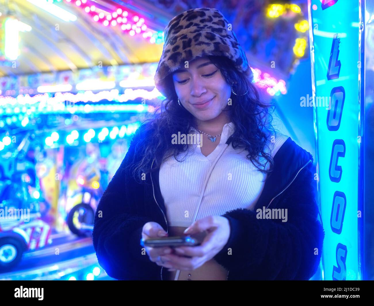 Smiling woman using the mobile next to a sign of a fairground ...