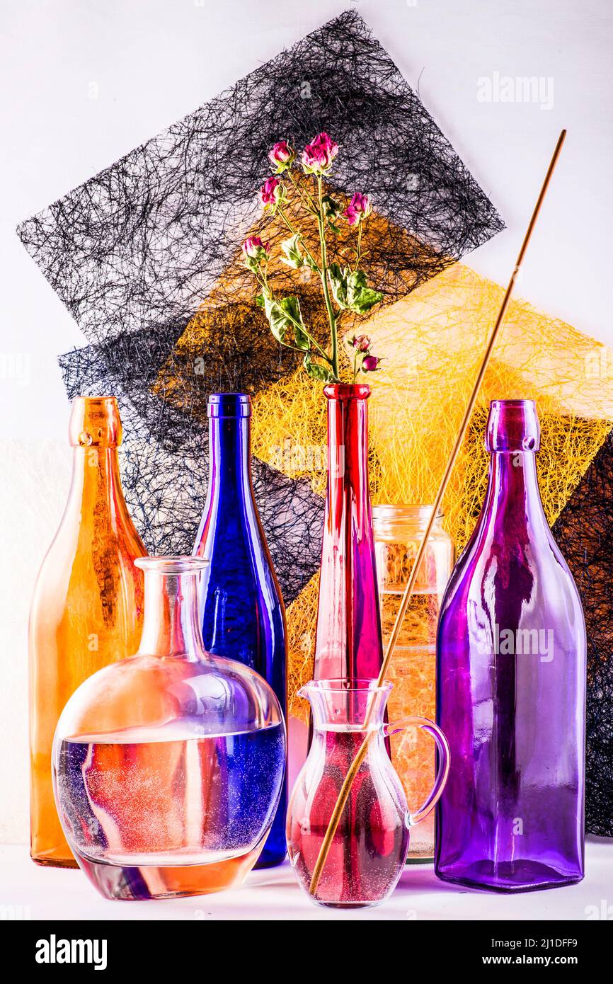 Still life with colored glassware and rose branch on an abstract ...