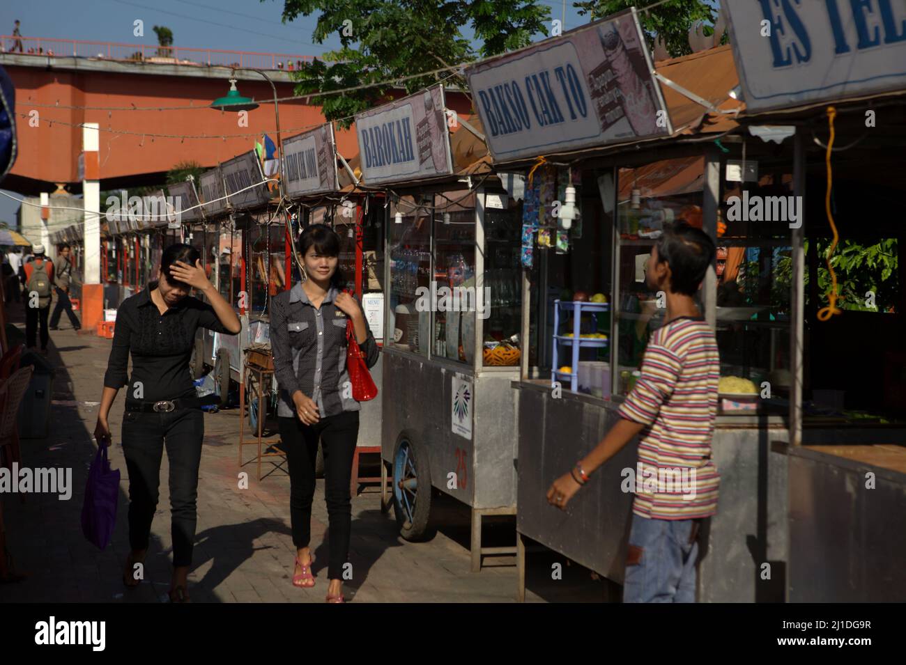 Young women walking on the sidewalk where a line of street food vendors ...