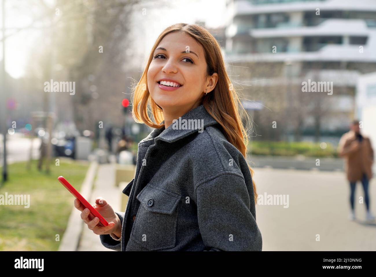 Relaxed girl looking back holding mobile phone with blurred city ...