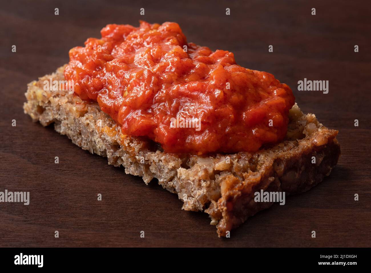 Ajvar spread on a slice of health bread on dark wood Stock Photo - Alamy