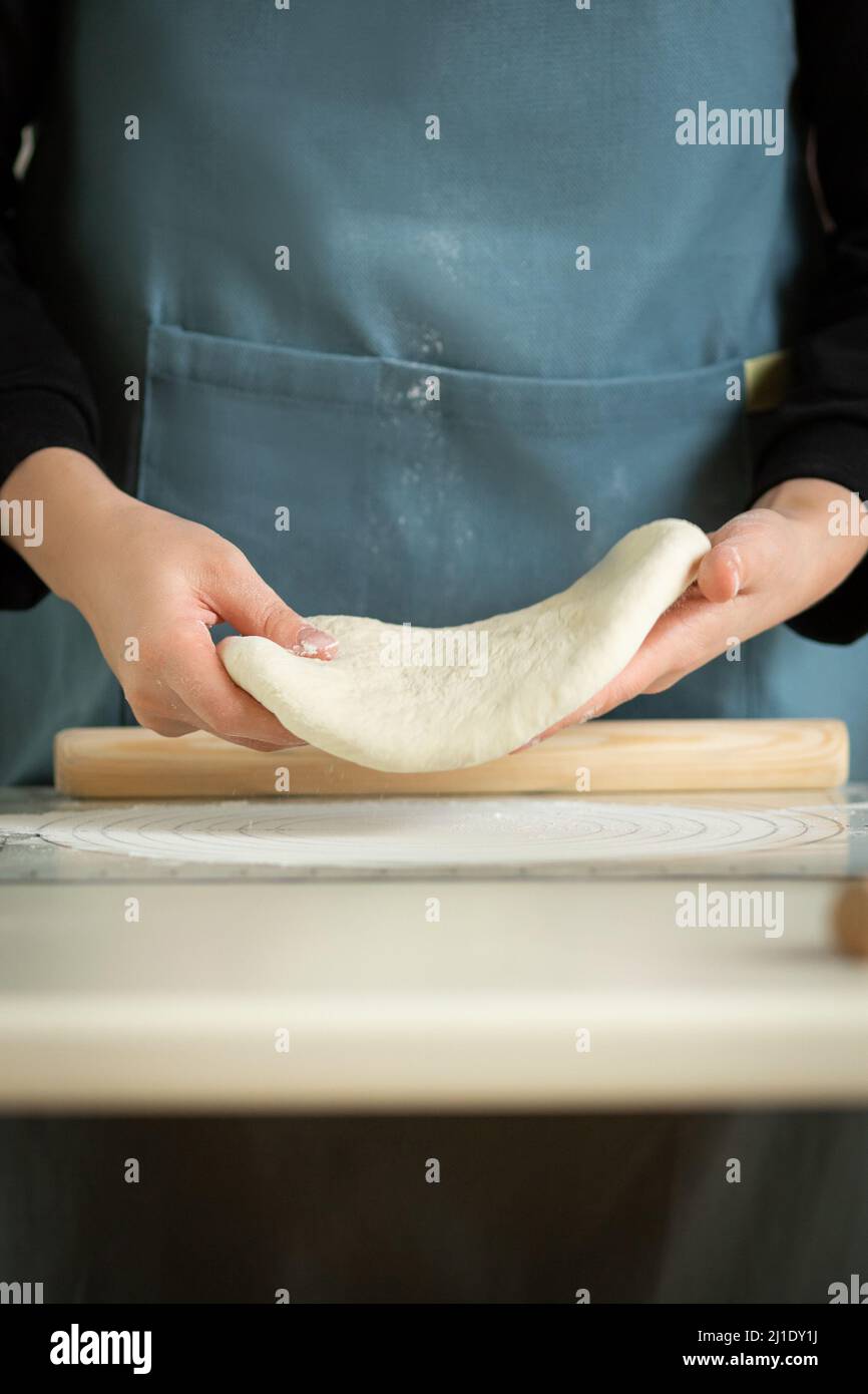 A cook in a blue apron holds a rolled out dough in his hands. Hand view ...