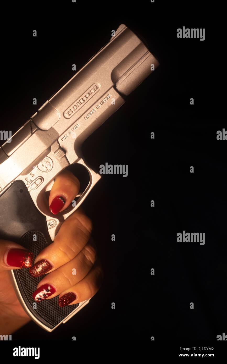 Lady spy detective with painted red nail varnish holding pistol gun at ...