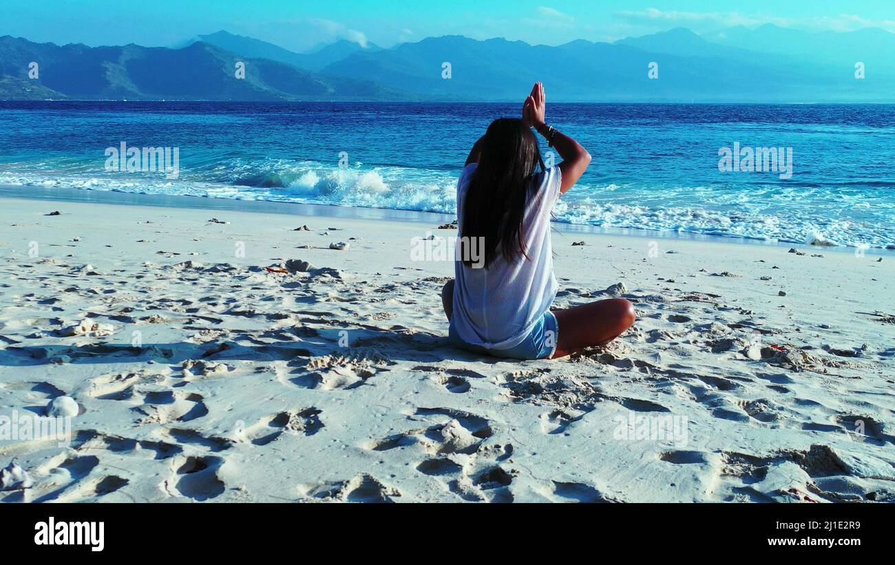 A Rear View Of A Sun Tanned Girl With Her Hands Up Sitting On The Beach
