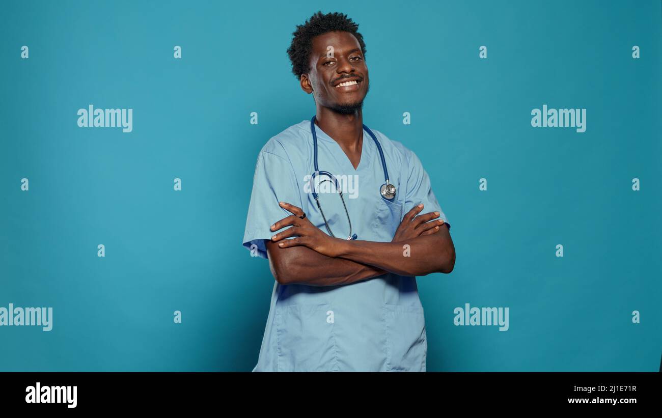 Positive nurse standing with crossed arms and smiling in studio ...