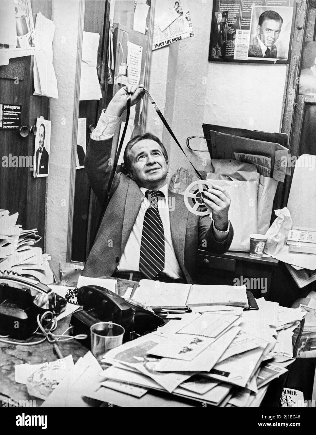 TV personality Joe Franklin examines a strip of film in his cluttered ...