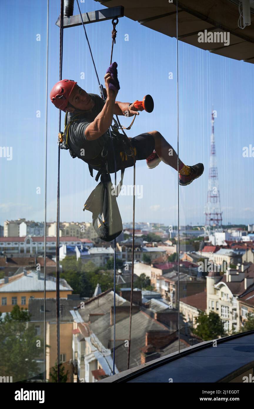Industrial mountaineering worker hanging on climbing rope and cleaning ...