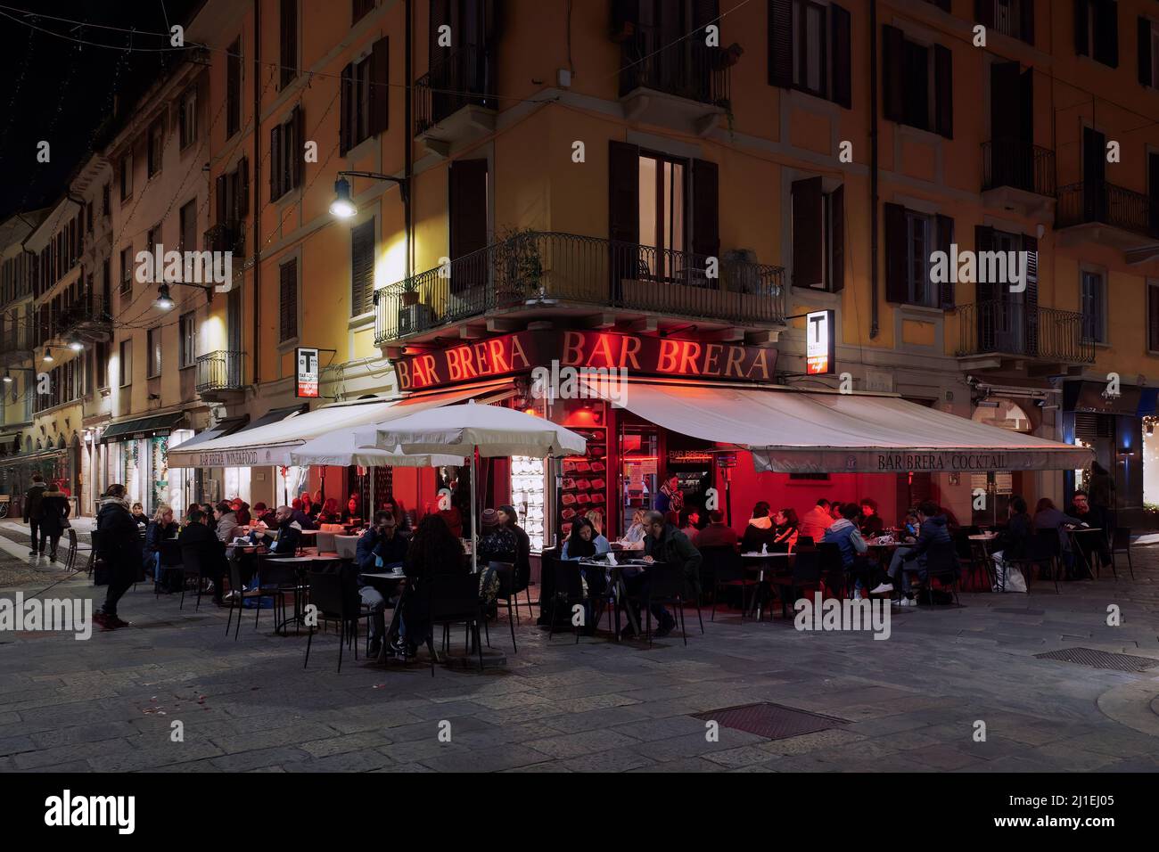 Milan, Italy night view of crowd in typical outdoor cafe restaurant with illuminated sign in ...