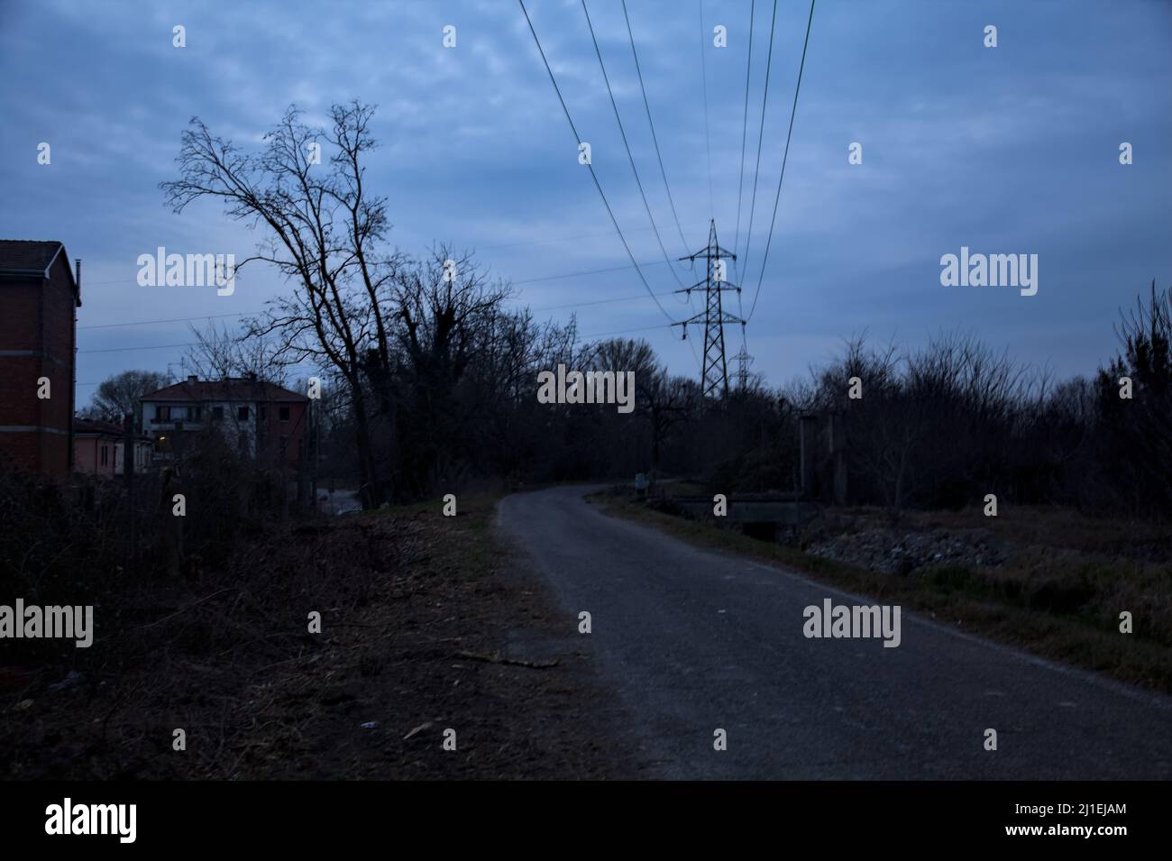 Road in the countryside with a gate at its edge on a cloudy day at dusk ...
