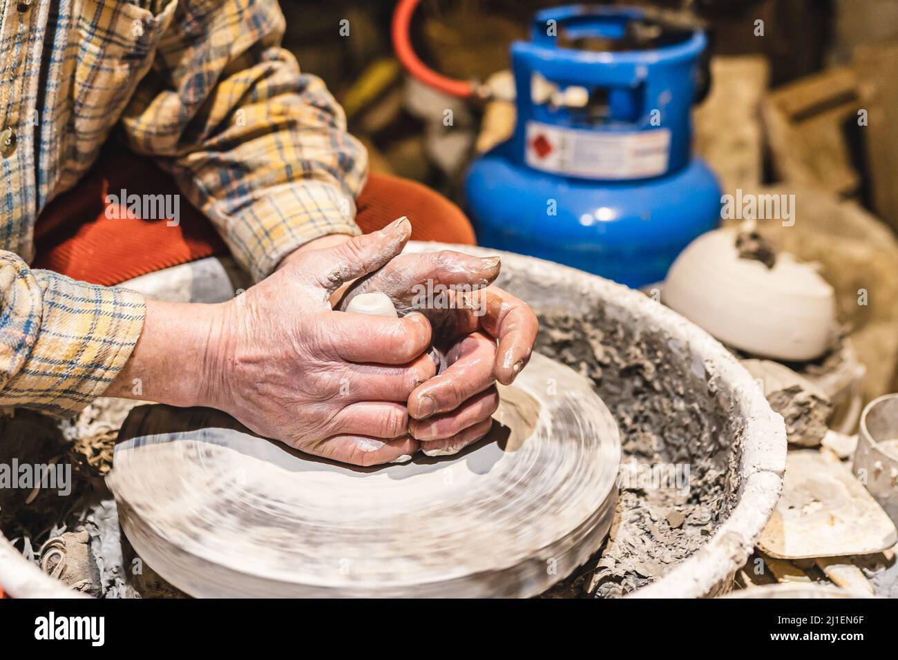 Muscular hands of middle-aged man, potter, soiled in clay, form pottery ...