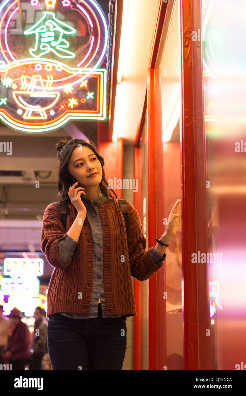 Young female tourist talking on the phone outside window of night ...