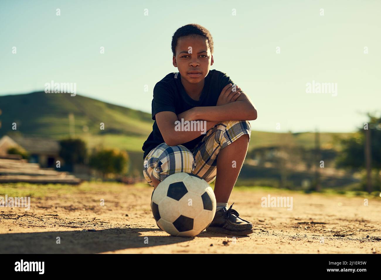 He loves the beautiful game. Portrait of a little boy crouching on a ...