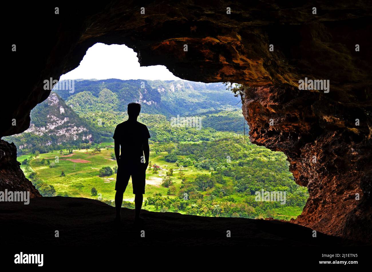 Adventurous tourist men looking through a cave opening through green ...