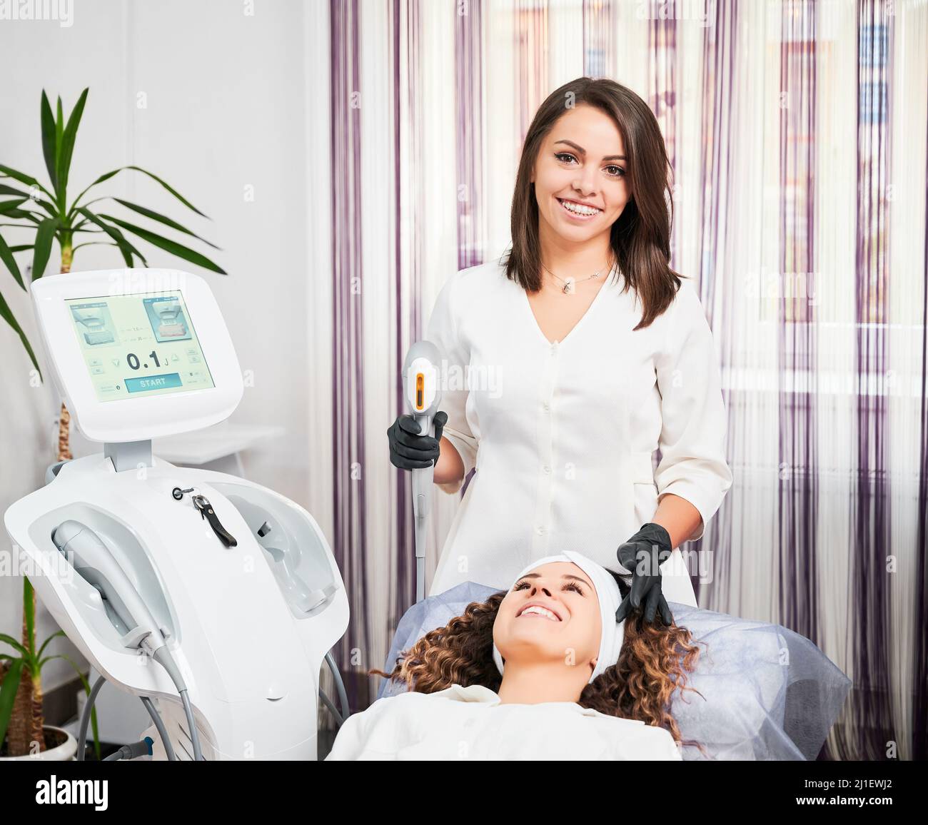 Smiling beautician standing near patient and holding special machine ...