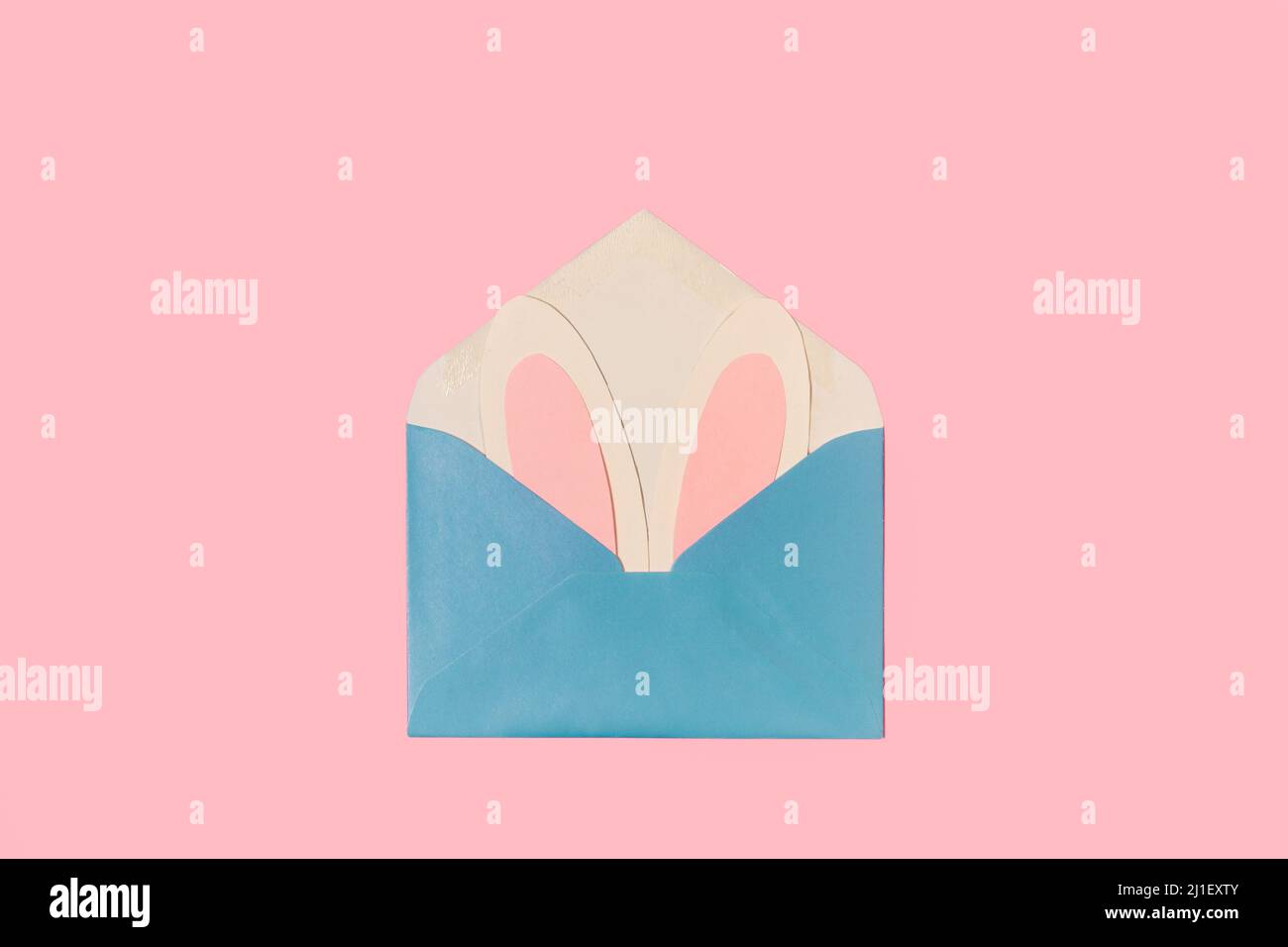 Paper rabbit ears in a blue envelope on a pink background with copy ...