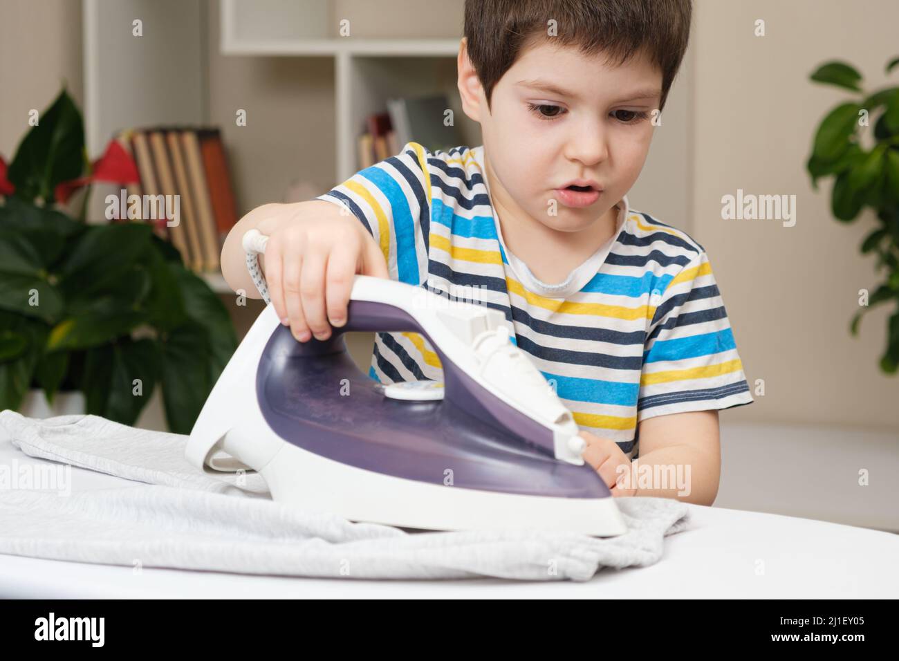 A boy of 4 years learns to hold an iron, iron clothes on an ironing ...